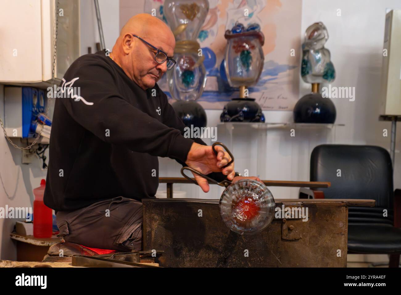 The glassblower grasps the glass with shears prior to breaking it off ...