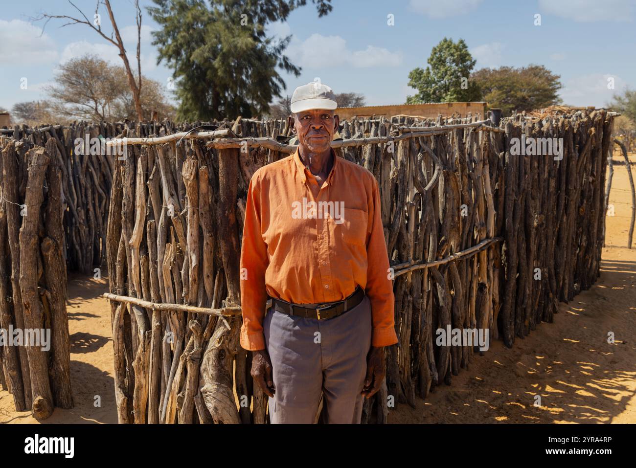 village african old man outdoors in the yard, wooden fence in the ...