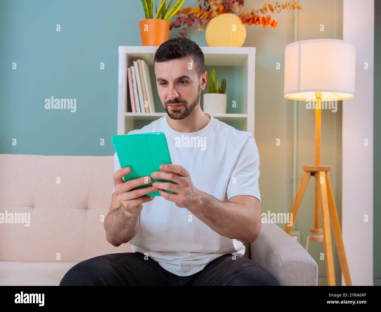 Man sitting on sofa, using tablet indoors in cozy, modern living room ...