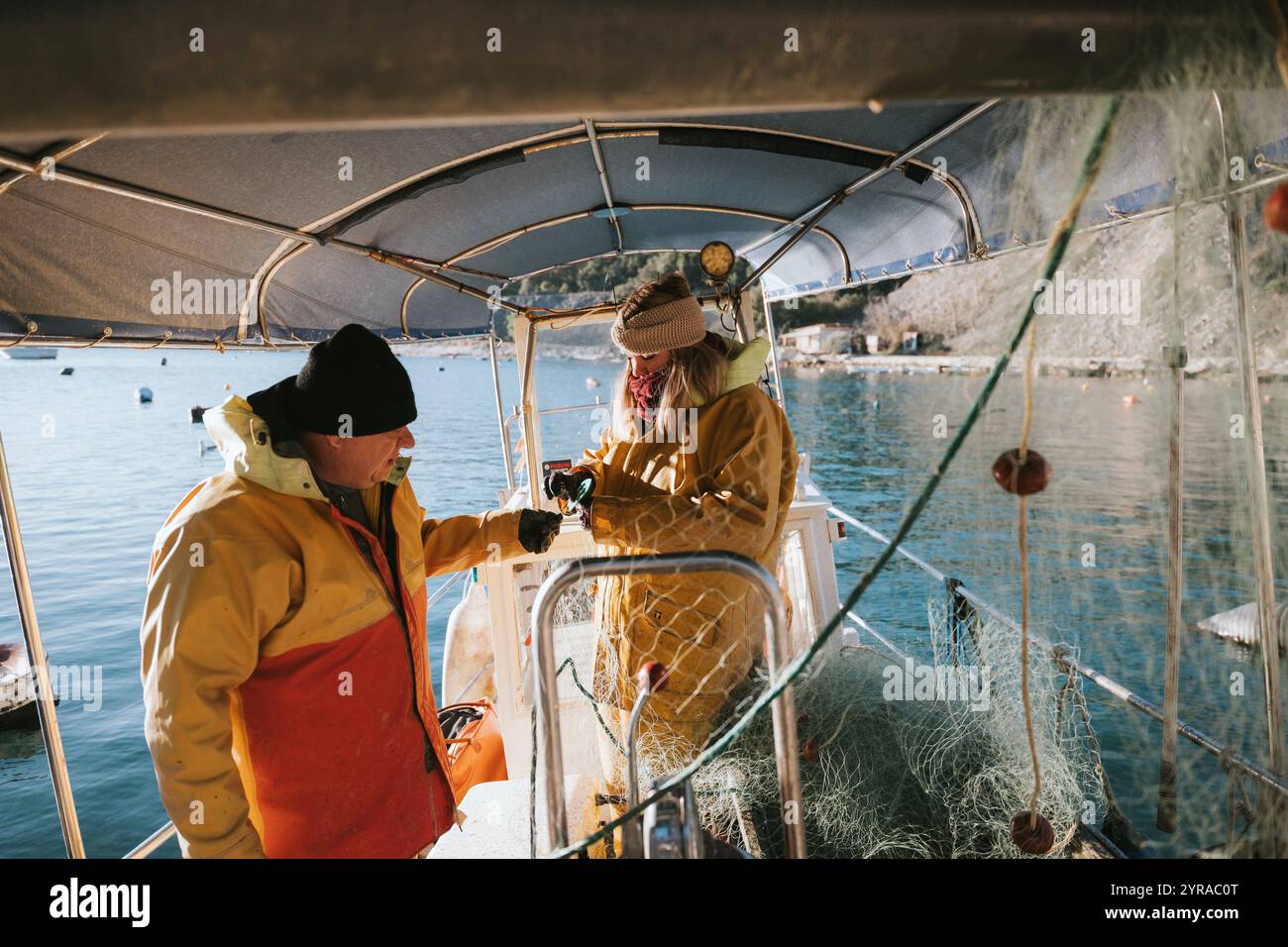 Young female fisherman in yellow oilskin untying nets with her father ...