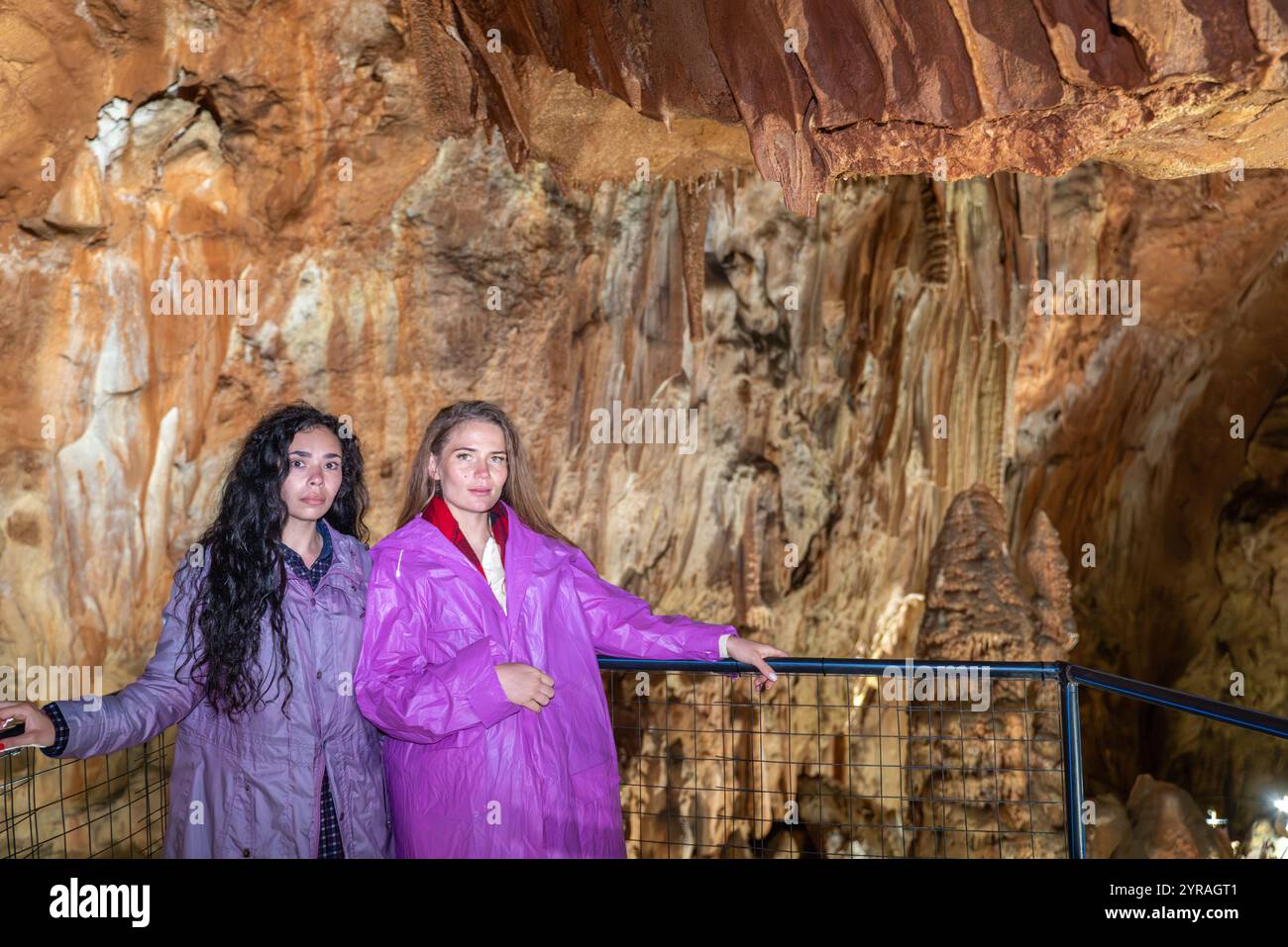 Two women standing in front of a cave with a railing Stock Photo - Alamy