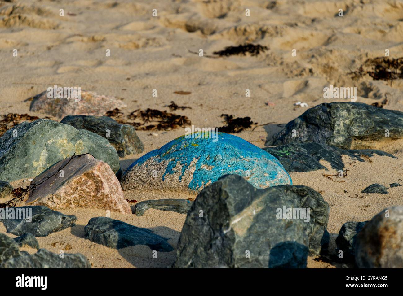 Single blue stone between natural stones at a sandy beach depicting ...