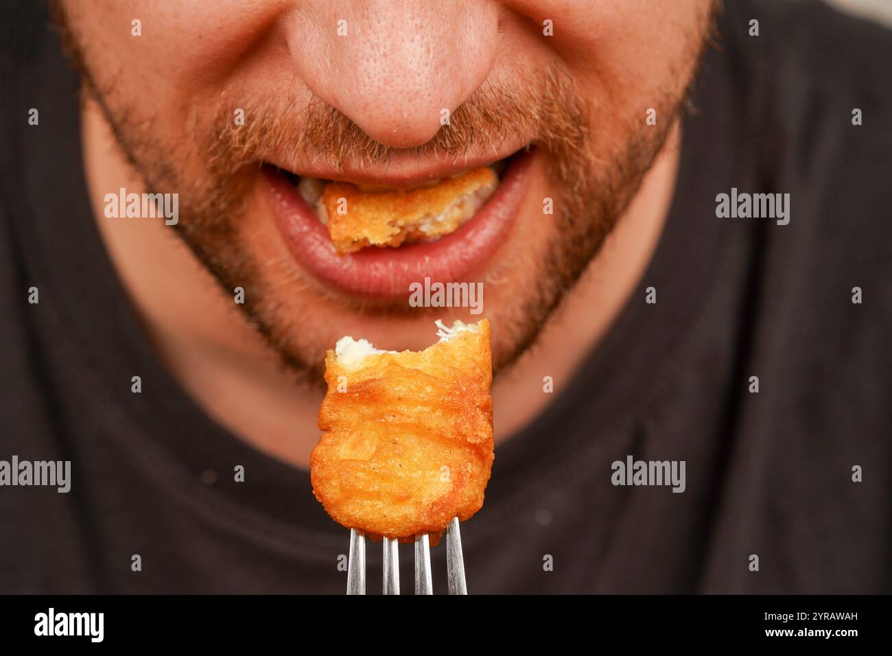 A close-up of a man eating a golden crispy nuggets highlights the ...