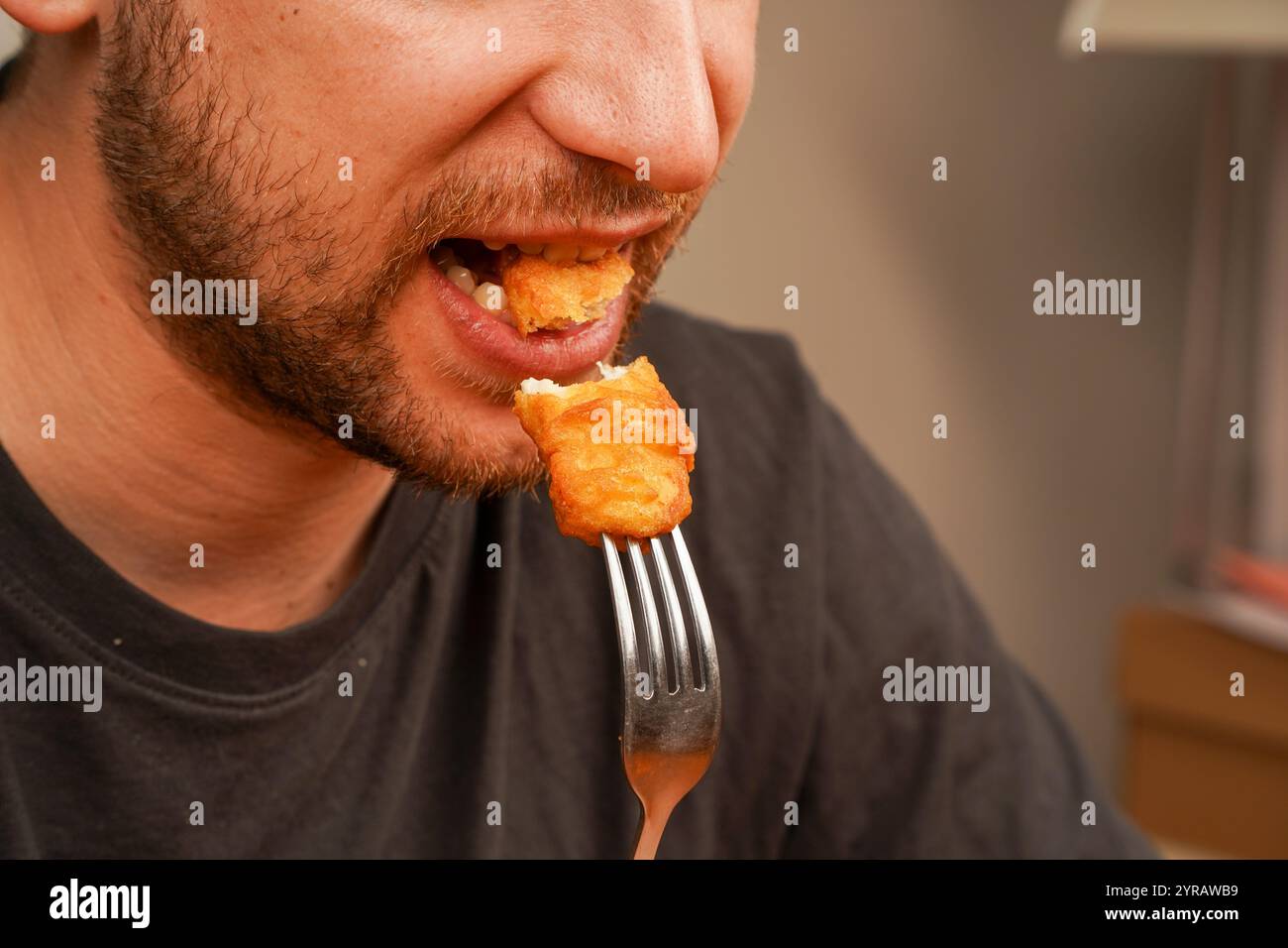 A close-up of a man eating a golden crispy nuggets highlights the ...