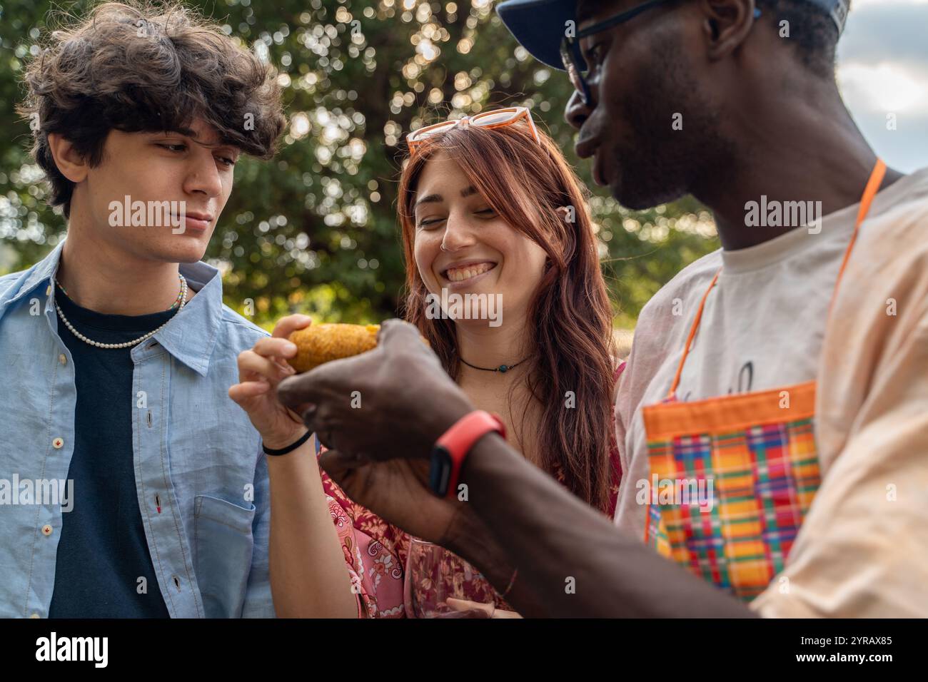 Candid moment of Gen Z friends laughing and sharing food outdoors ...