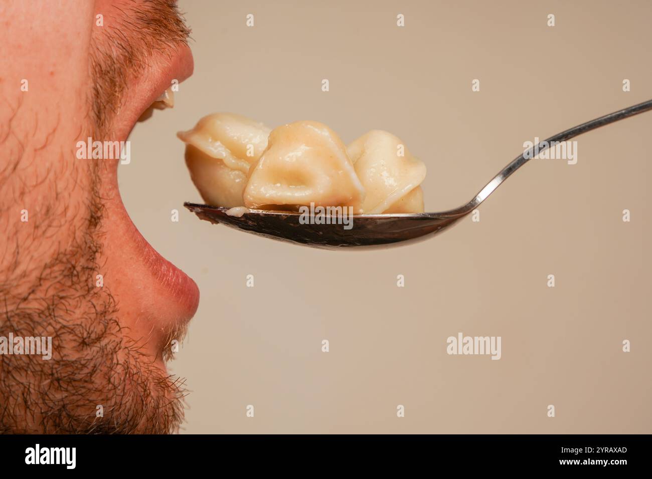 A delicate dumpling, lifted on a spoon near an open mouth, demonstrates ...