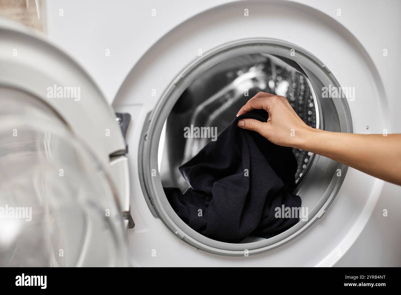 Woman putting black cotton clothes into the washing machine, close-up ...