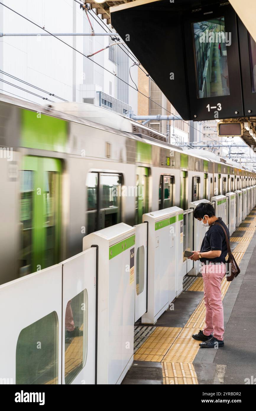 Man using his mobile phone while waiting on Otsuka station platform on ...