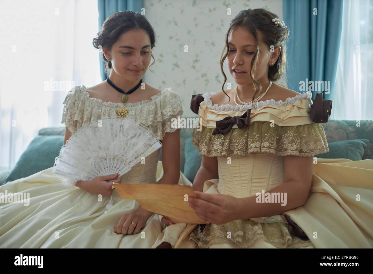 Front view portrait of two young ladies reading letter together sitting ...