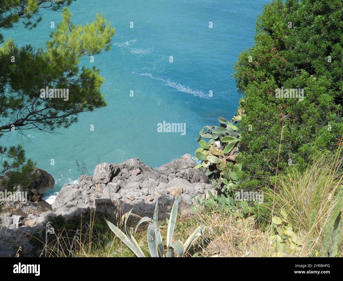 A breathtaking coastal view reveals vibrant turquoise waters lapping against rugged rocky ...