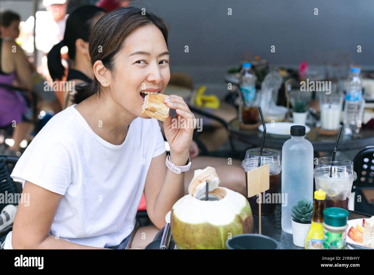 Happy asian woman eating tuna sandwich at local cafe outdoors Stock ...