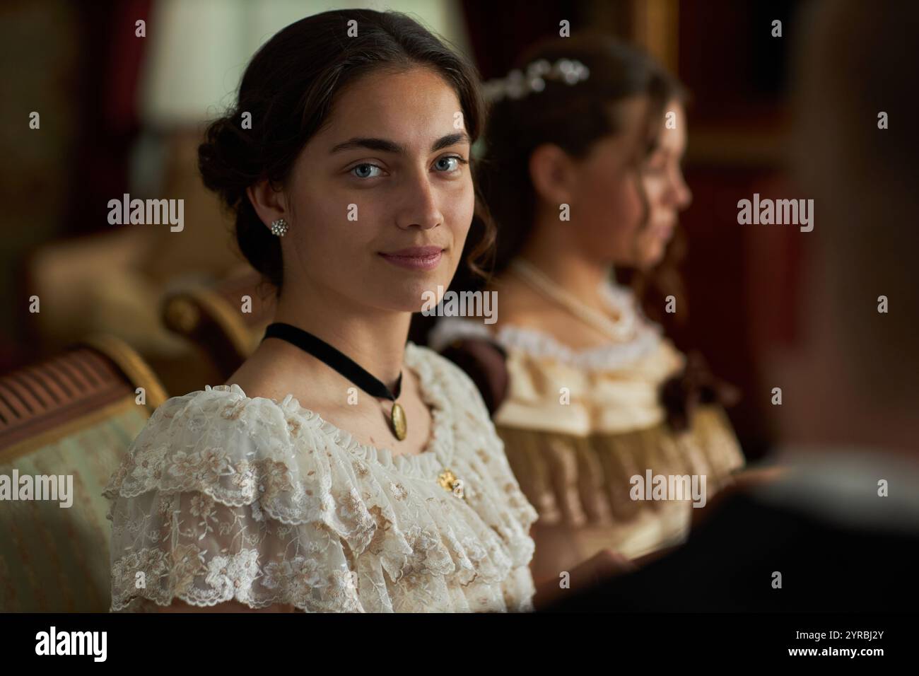 Portrait of young woman wearing lace gown gazing softly at camera with ...