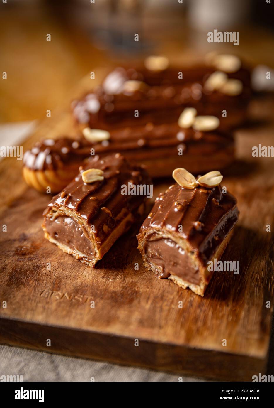Chocolate eclairs topped with peanuts are placed on a wooden cutting ...