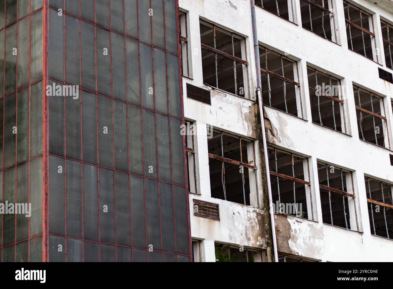 An abandoned industrial building featuring broken windows, peeling facade, and a contrasting red ...
