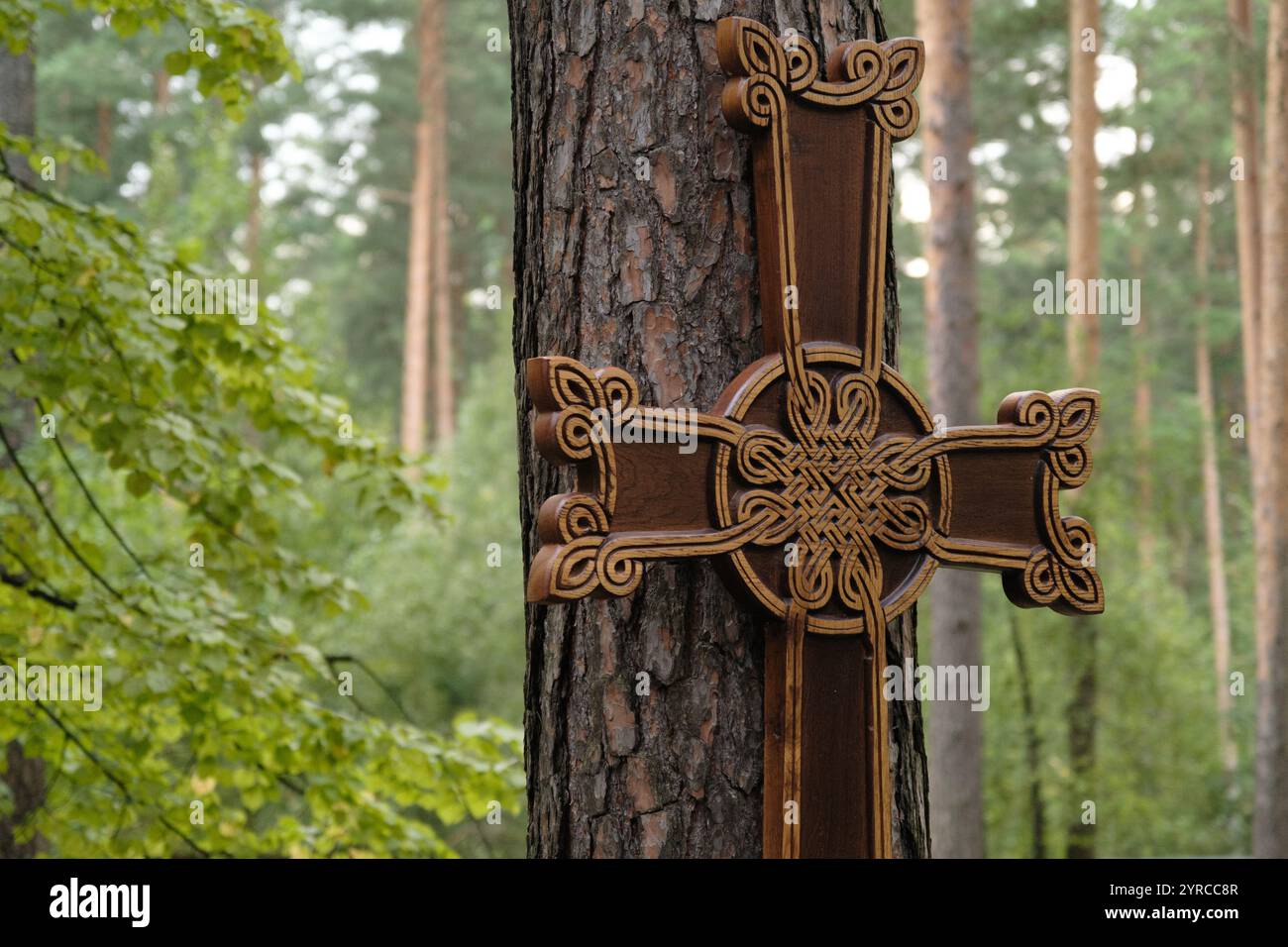 A beautifully carved wooden cross attached to a tree in a serene forest cemetery, surrounded by ...