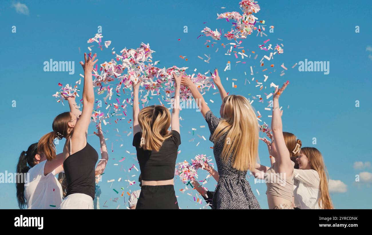 Group of friends throwing confetti in the air while partying outdoors ...