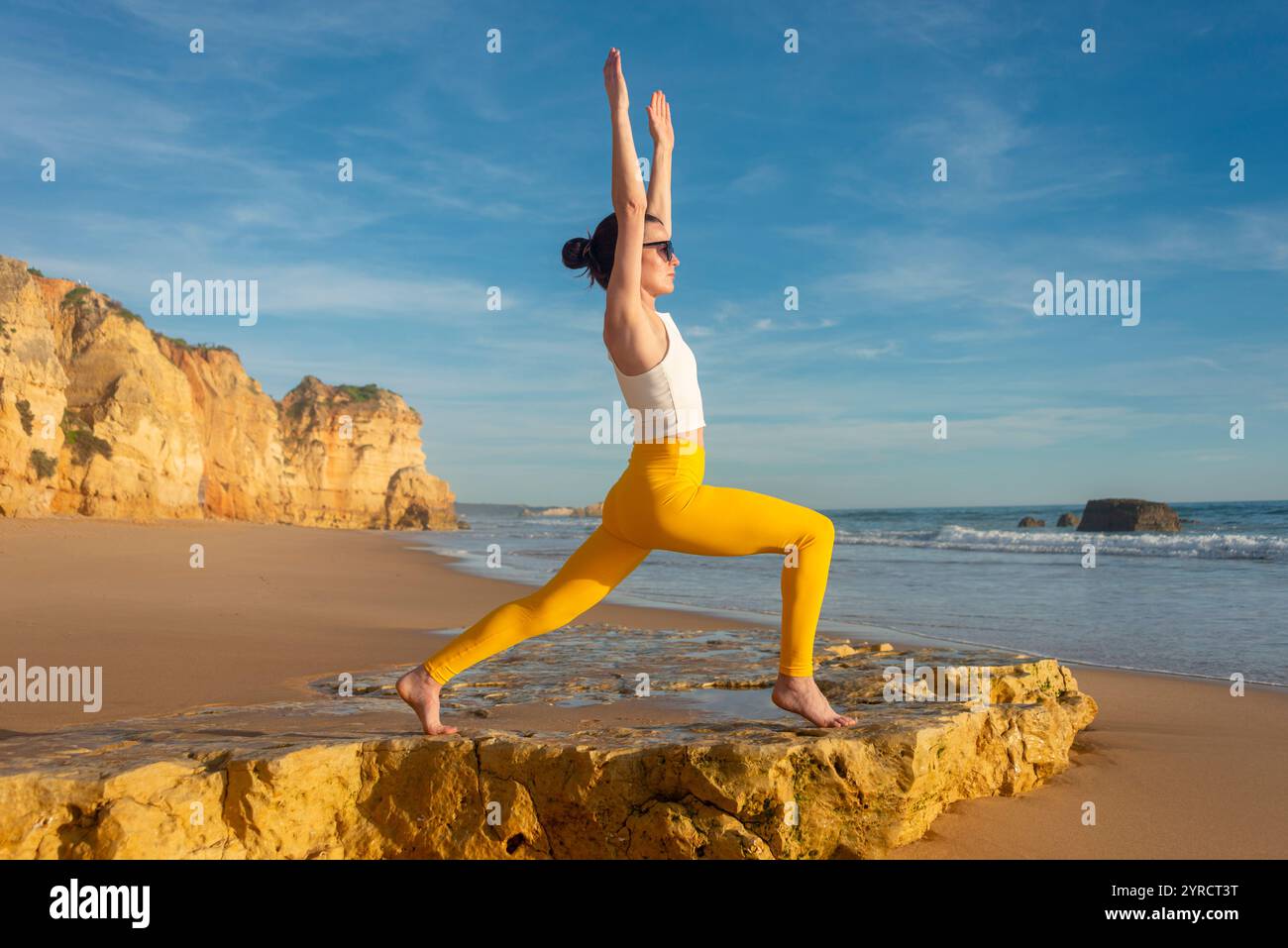 Woman doing a high lunge, crescent yoga pose on the beach in the sun ...