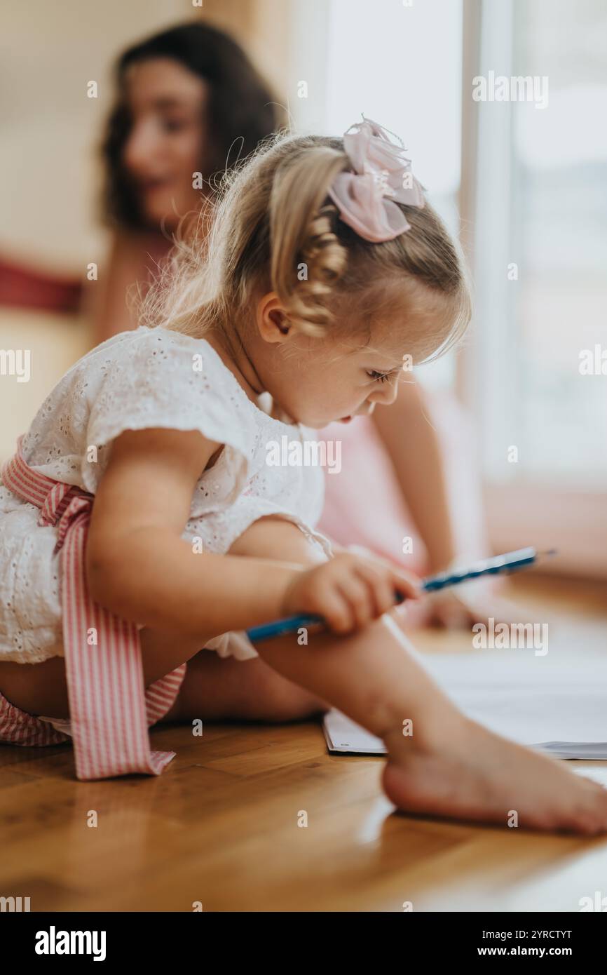 Little girl drawing with mother and sister in the background, family ...