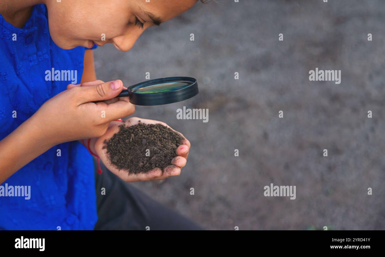 A child looks at the soil through a magnifying glass. Selective focus ...