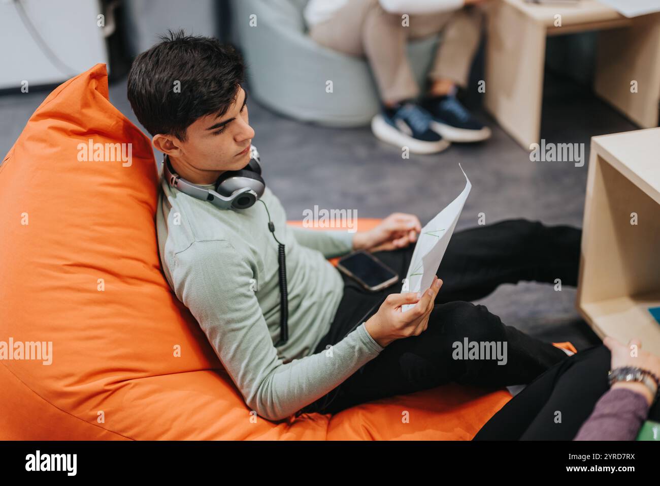 Student relaxing in a modern school setting while reading papers on an ...