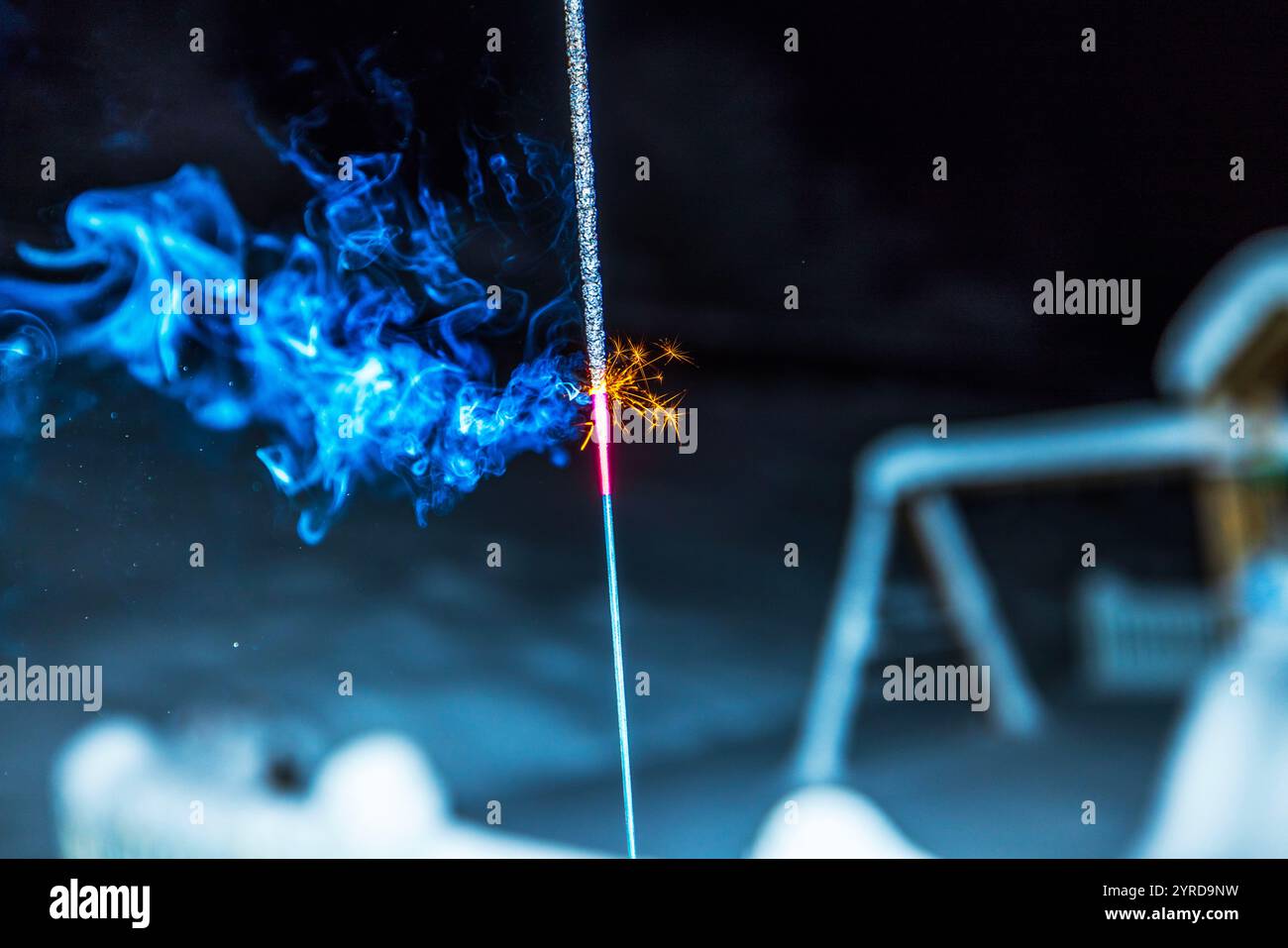 Sparkler emitting orange sparks with swirling blue smoke glowing in ...