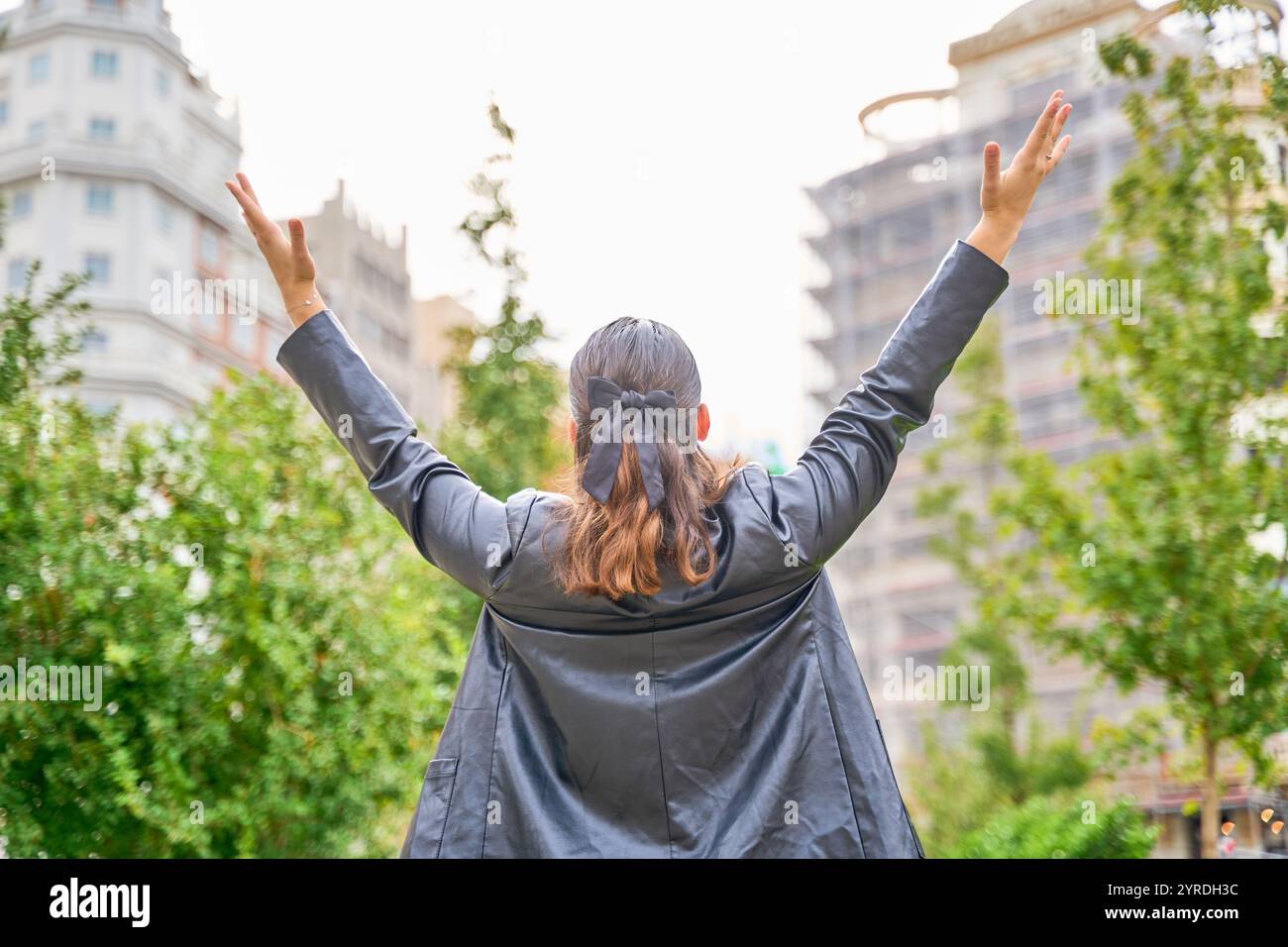 Woman raising her arms with her back to the camera in an urban park ...