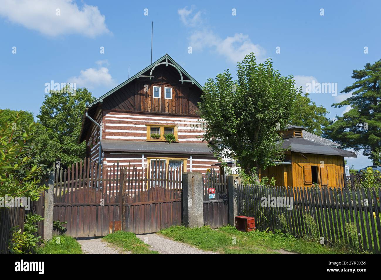 Two-storey wooden house with fenced garden surrounded by trees and blue ...