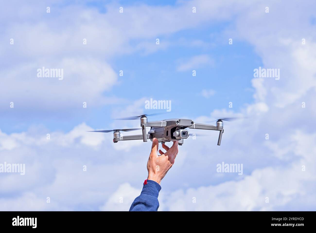 Hand holding a quadcopter drone against cloudy blue sky. Hand Launching ...