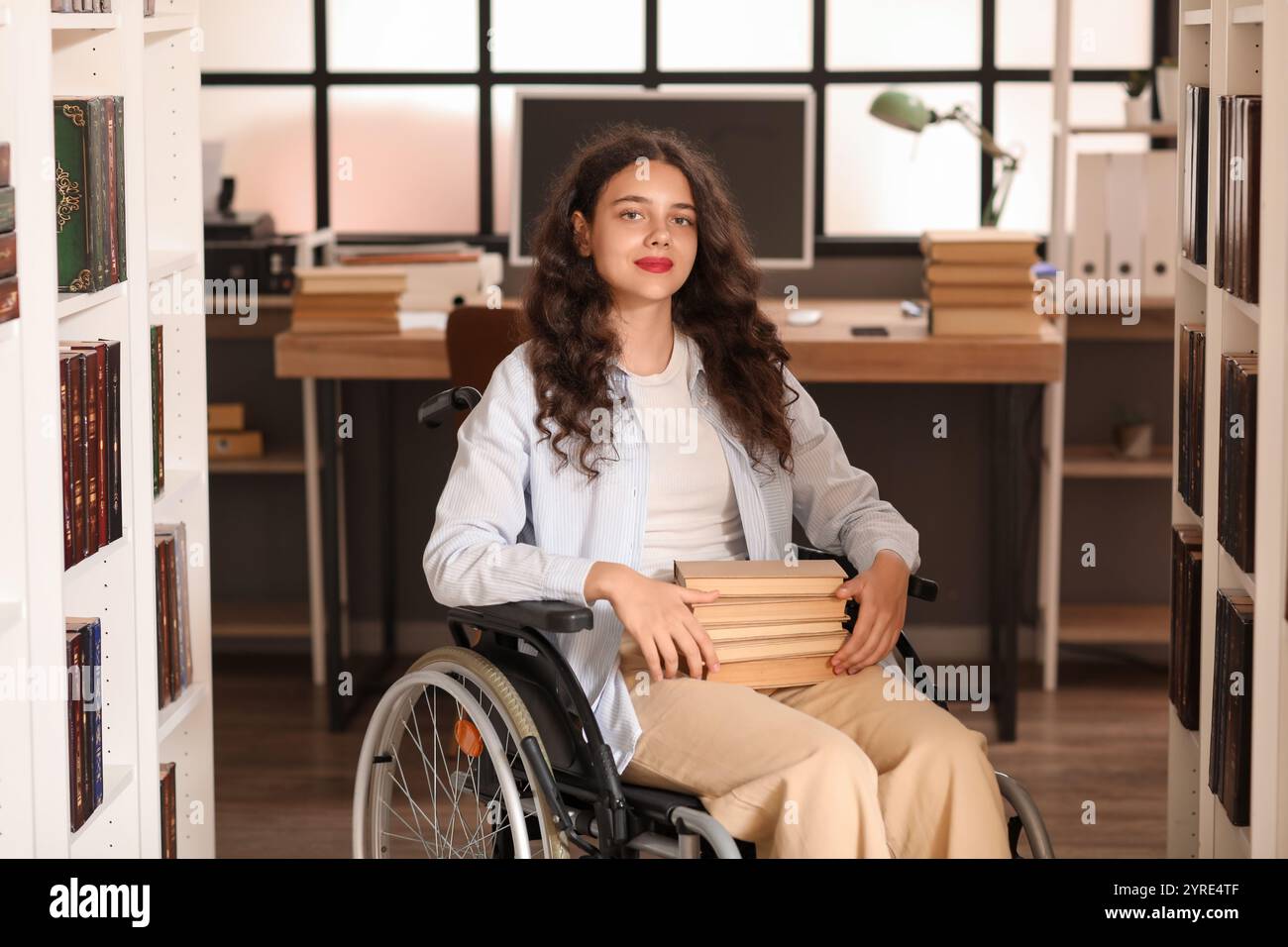 Female student in wheelchair with stack of books in library Stock Photo ...