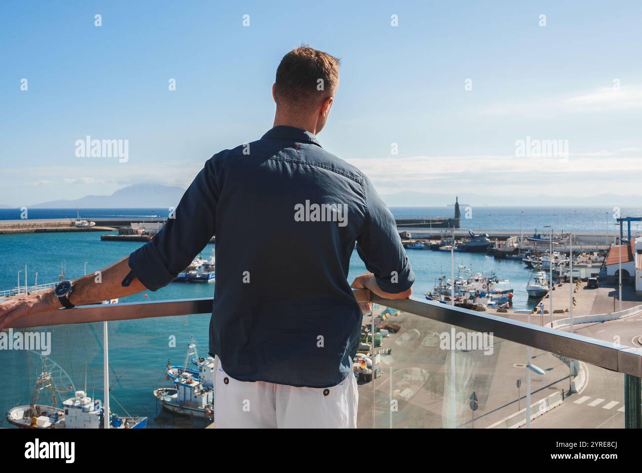 Man on Balcony Overlooking Marina with Lighthouse and Mountains Stock ...