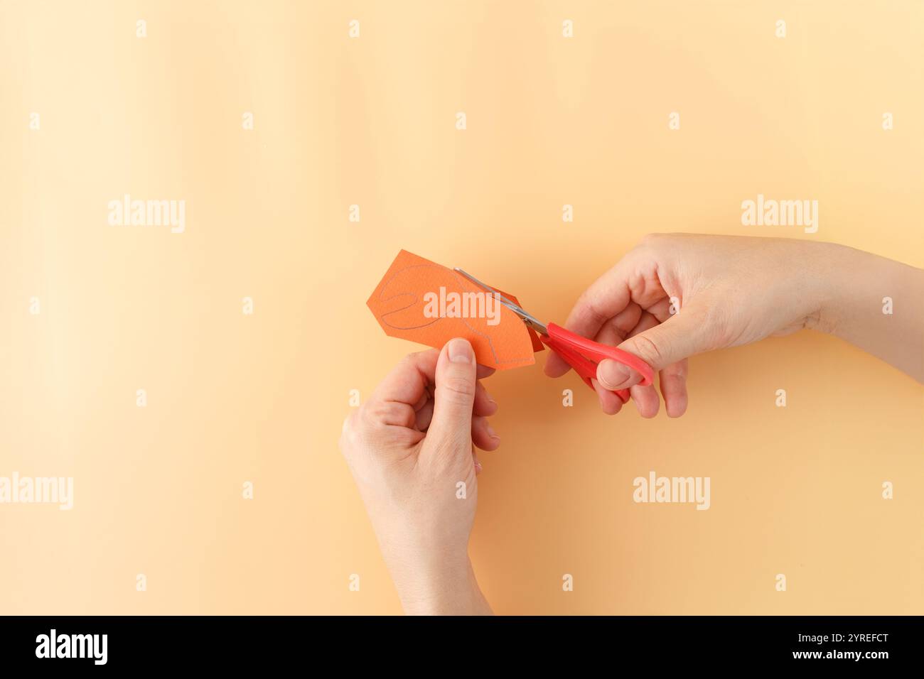 Hands cutting orange paper into crab claw shape with red scissors on a ...