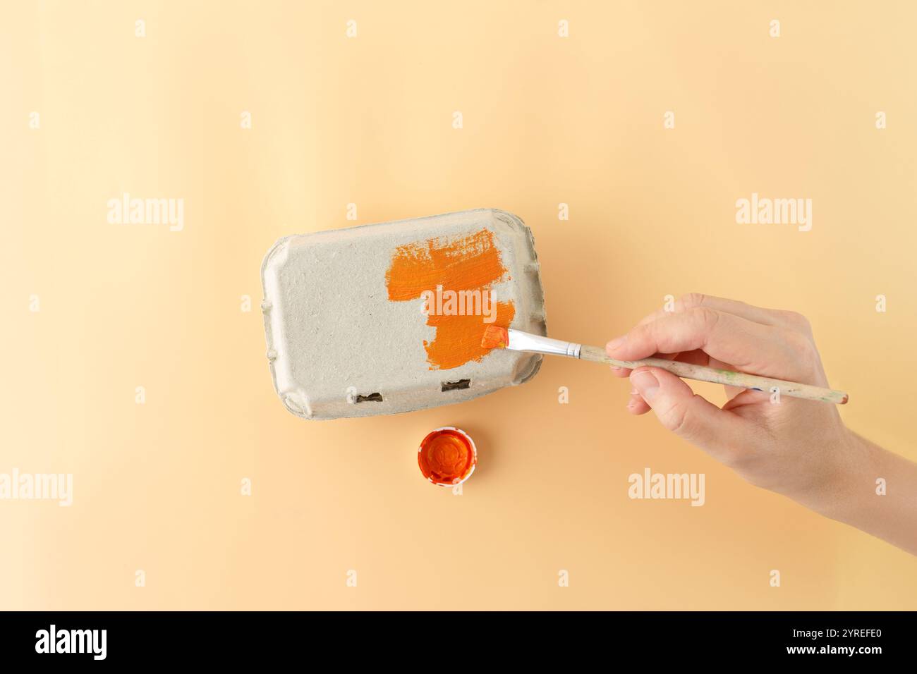 Painting an egg carton orange with a brush for a DIY craft project on a ...