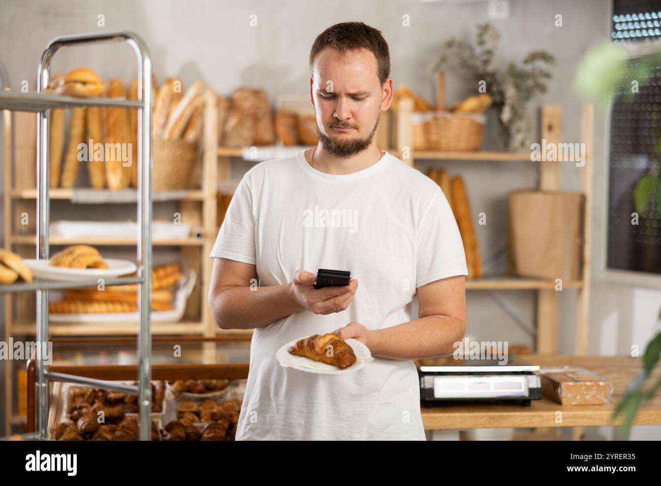 European male customer with phone takes pictures of croissant in ...