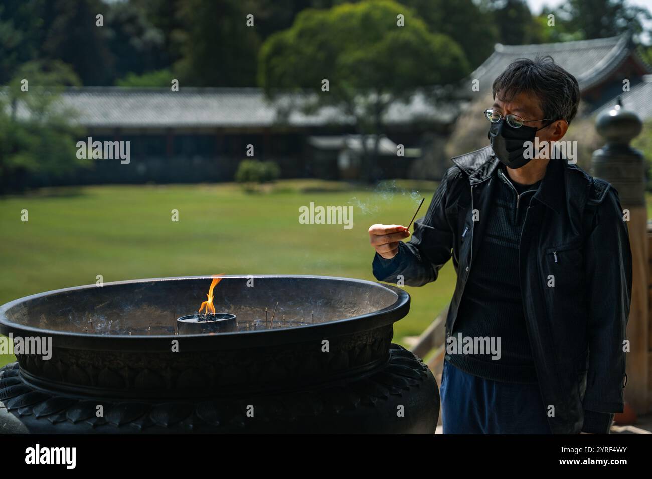 A man lights an incense stick in a peaceful Japanese temple, creating a ...