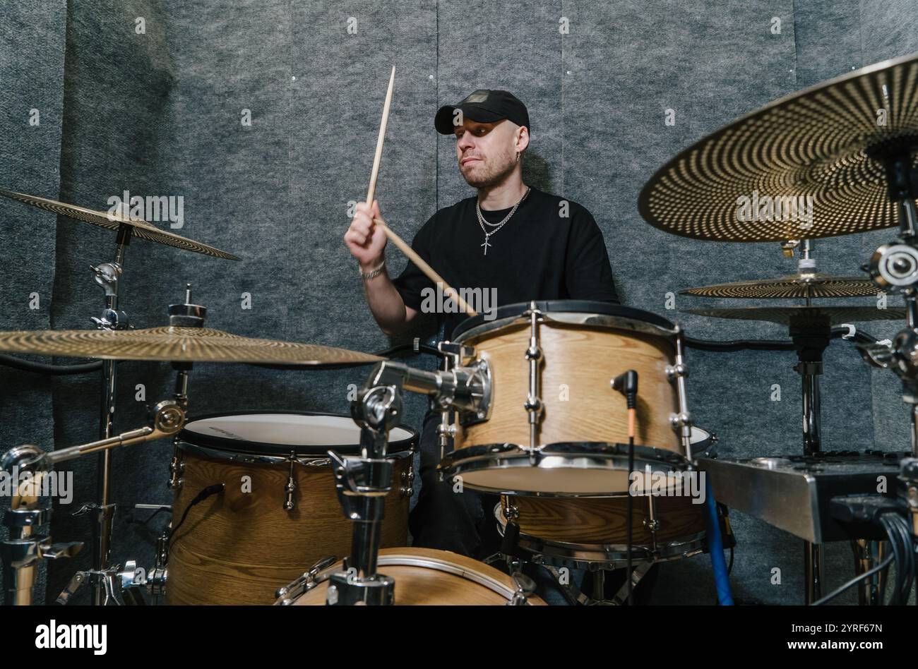 Drummer in black cap performing on wooden drum kit in soundproof music ...