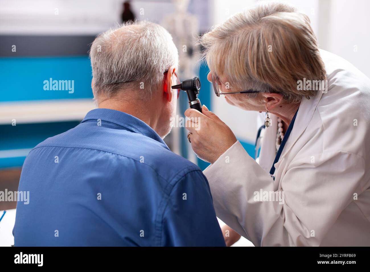 Male pensioner patient in hospital room has his ear examined by skilled ...