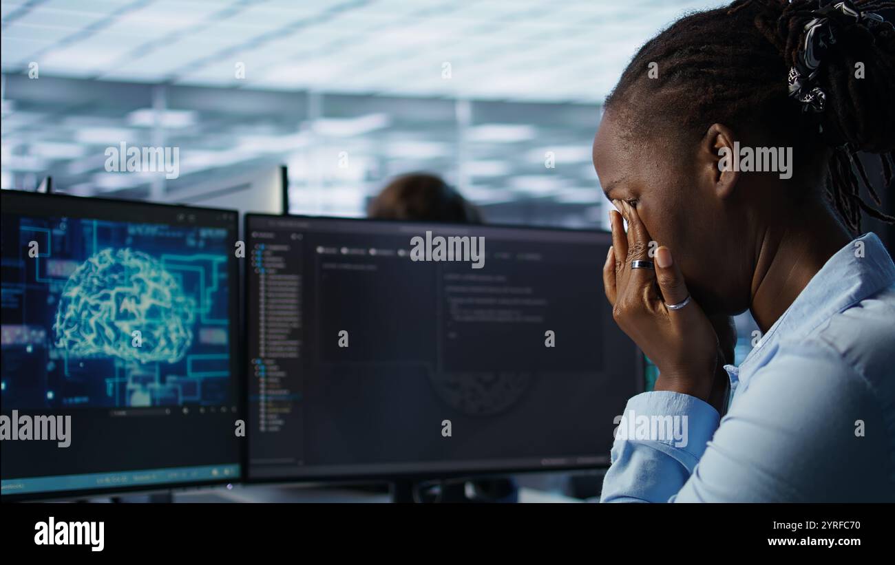 Tired software developer having eye strain while working on high tech data center computer ...
