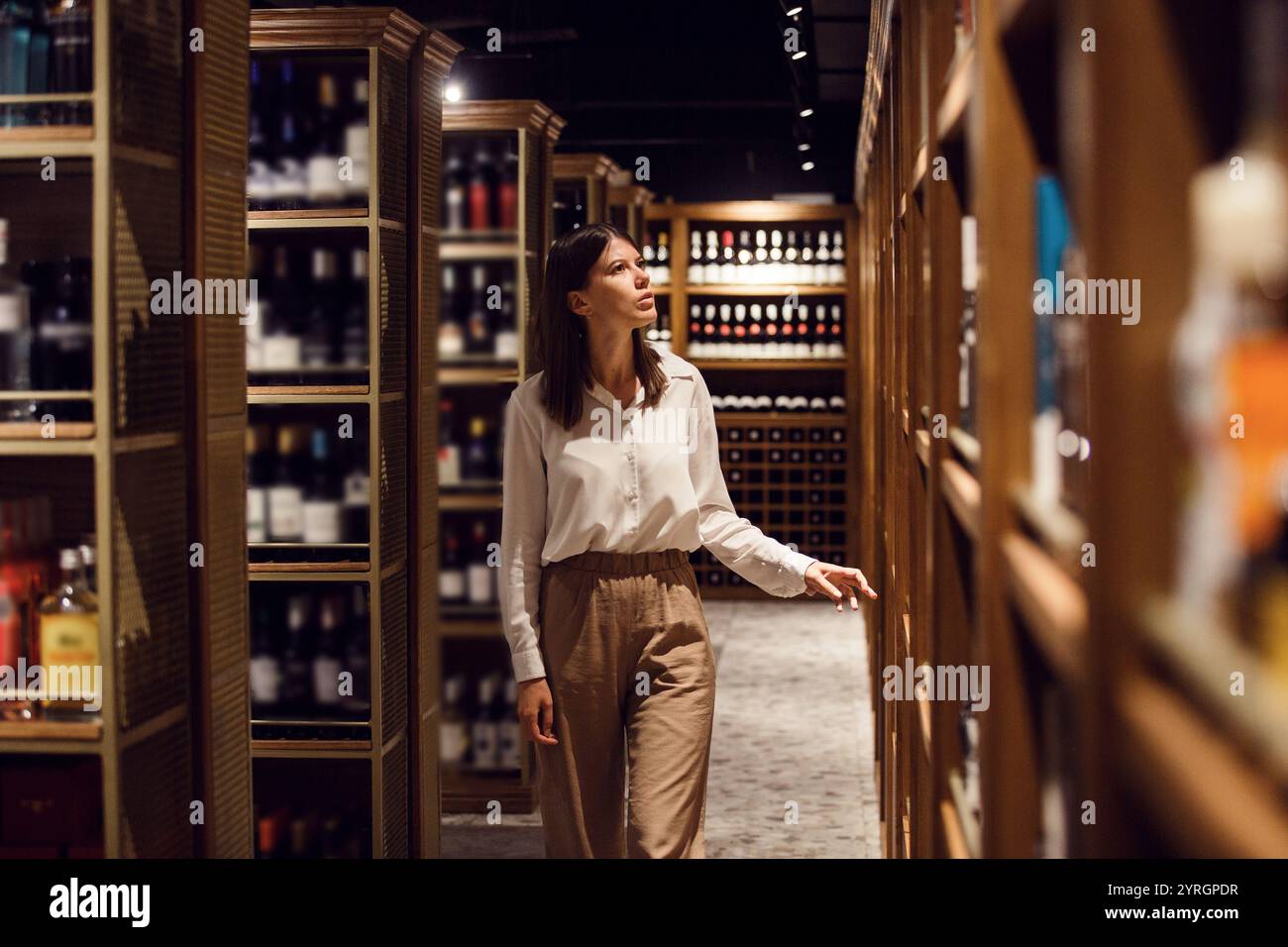 Professional female wine expert chooses wine in cellar among many ...