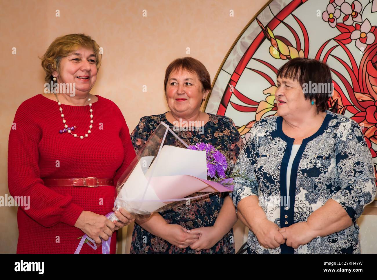 Three Russian friends, aged 60 and 70, hold a bouquet of flowers and ...