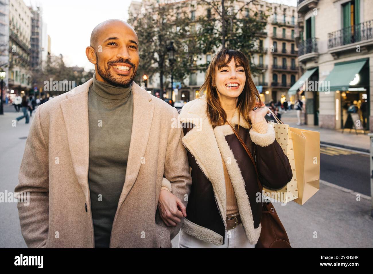 A joyful couple walks arm in arm with shopping bags in an urban setting ...