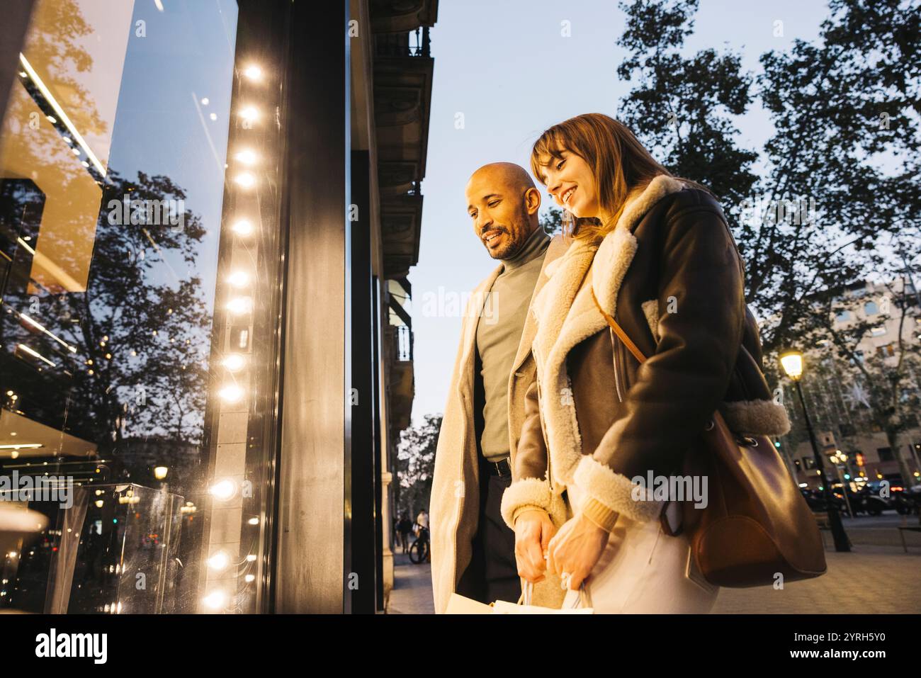 A cheerful couple looking at a window shop in the city, exploring ...