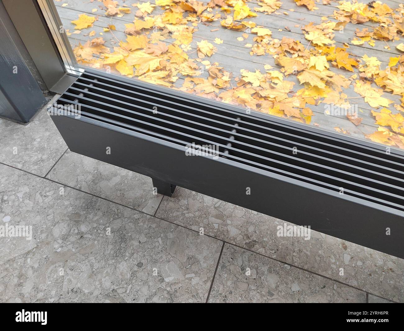 A modern floor heating vent near a glass window with autumn leaves ...