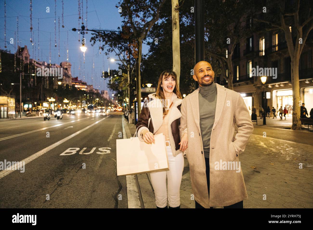A cheerful couple stands on a bustling city street at night, searching ...