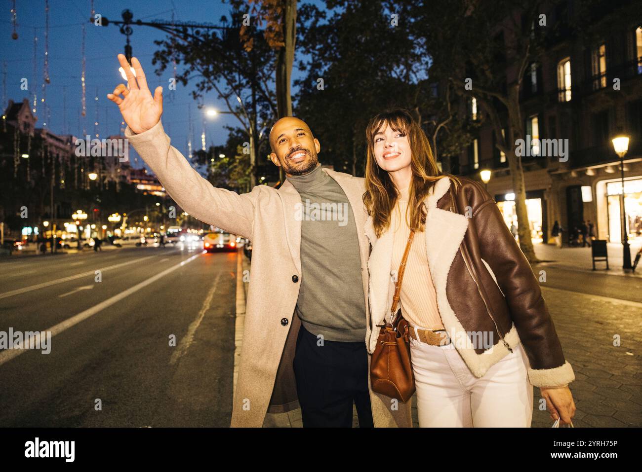 A cheerful couple standing on a bustling city street, trying to hail a ...