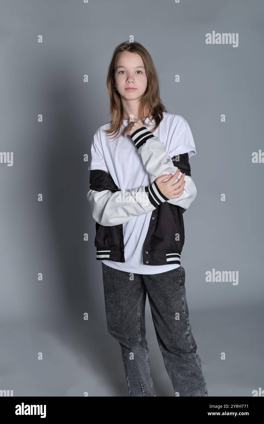 A teenage girl gazes downward, gently holding her jacket in a casual ...