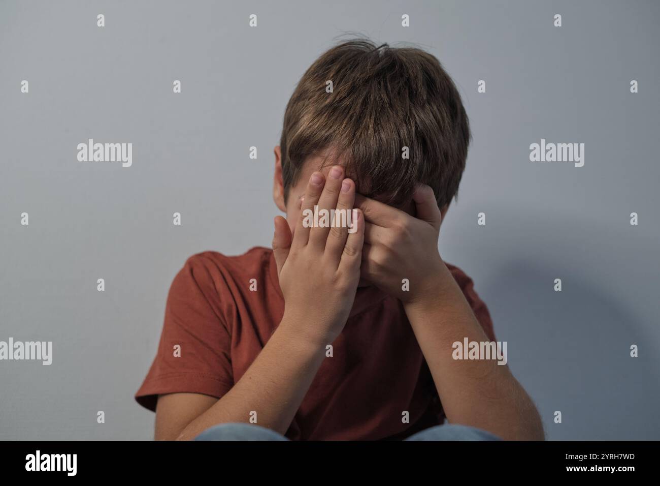 A boy covering his face with both hands, expressing a moment of shyness ...