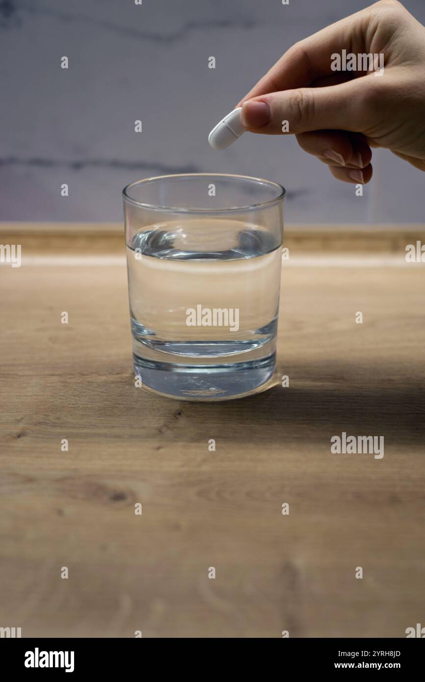 female hand drops a dissolving into a glass of water. health care ...