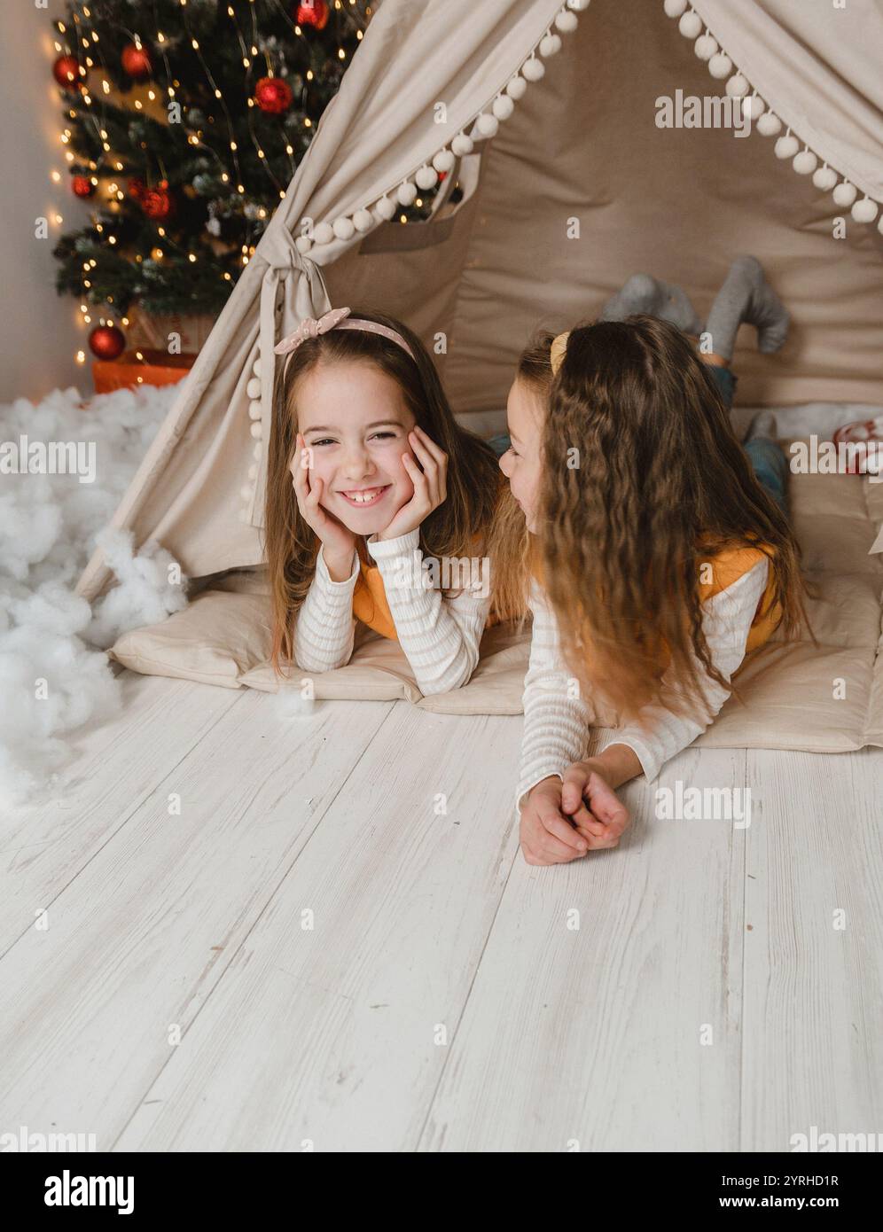 Two happy sisters share a magical Christmas moment inside a cozy teepee ...