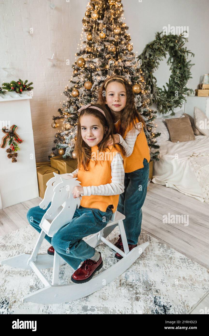 Two sisters enjoy a cozy Christmas moment, sharing a rocking horse in ...