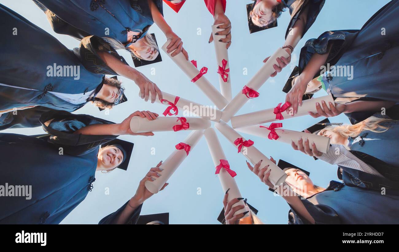 Group of young graduates forming a circle in the air holding their ...